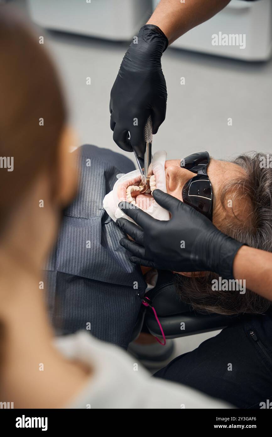 Dental surgeon and assistant remove a tooth from elderly woman Stock ...
