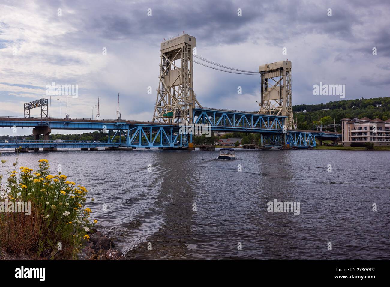 A double deck lift bridge crossing a river with a boat heading towards ...