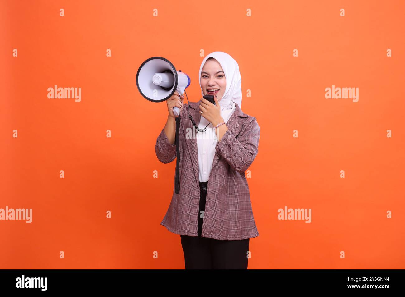 Cheerful young Asian woman in hijab facing front shouting using mic ...