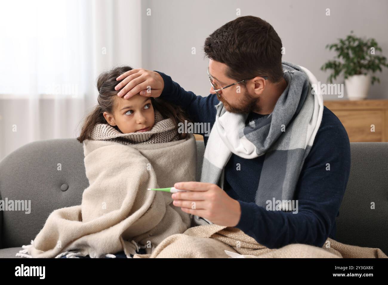 Cold symptom. Father with his daughter suffering from fever on sofa at ...