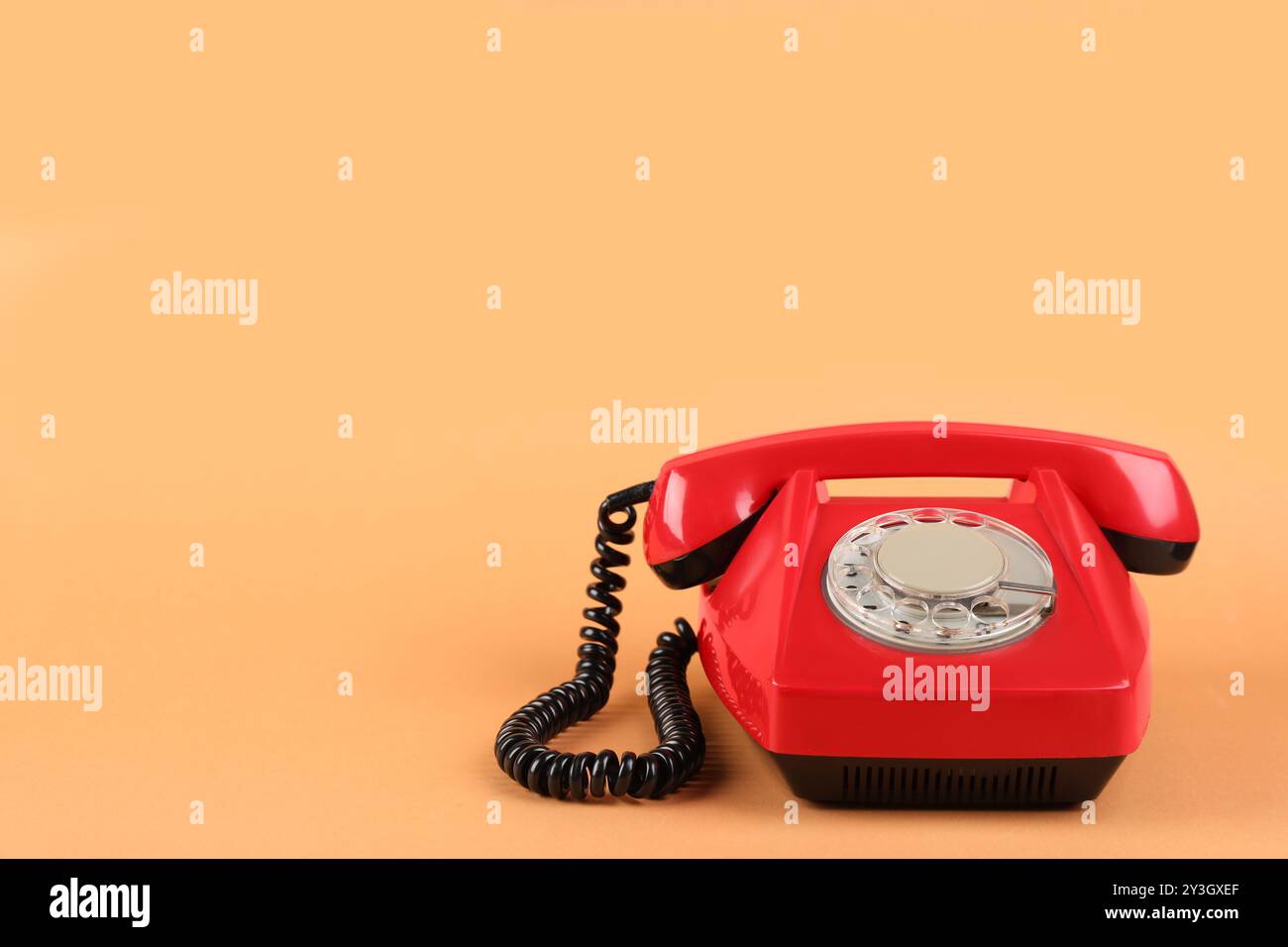 One red telephone with handset on pale orange background, space for ...