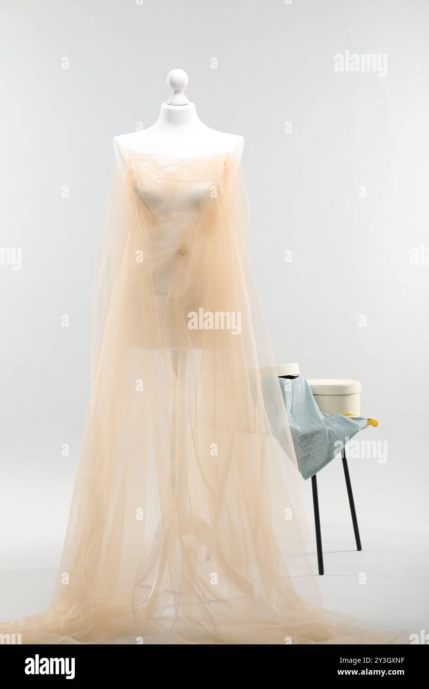 Mannequin with fabric and boxes on side table against light grey ...