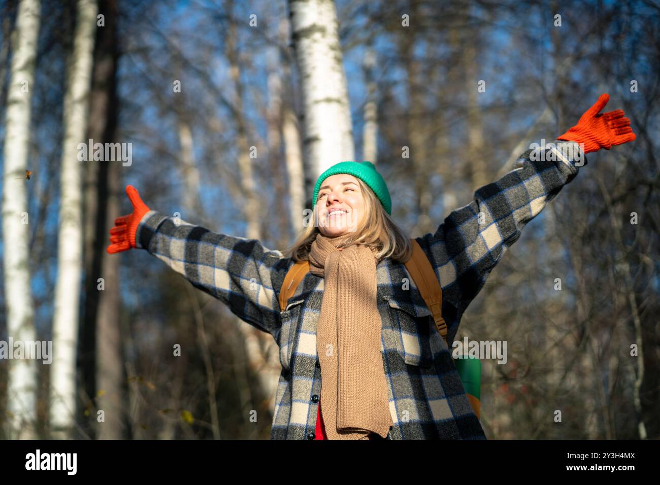 Happy middle aged traveler woman with arms raised in fall forest at sun ...
