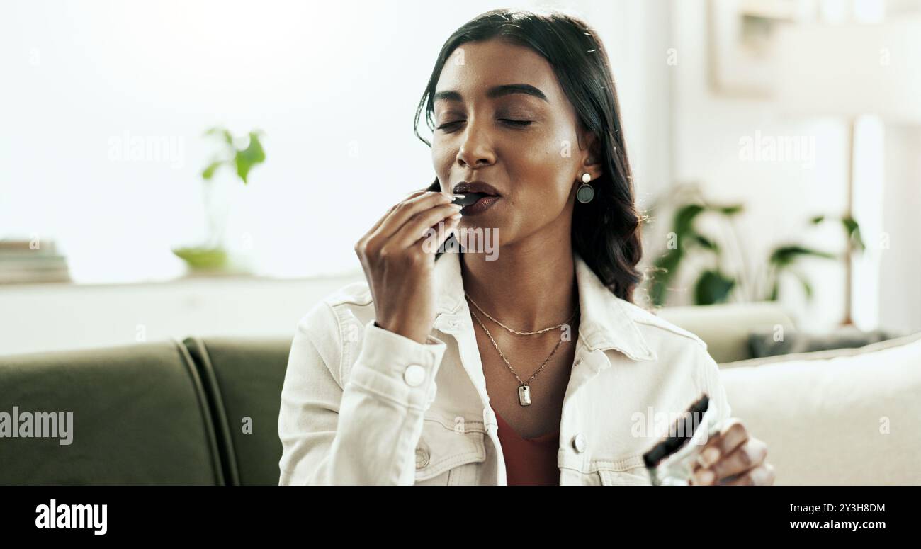 Chocolate, relax and smile with Indian woman on sofa in living room of ...