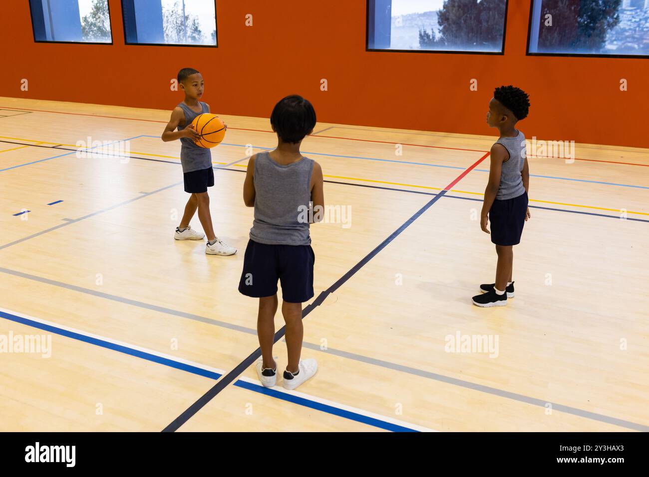 Playing basketball in school gym, three multiracial boys practicing ...