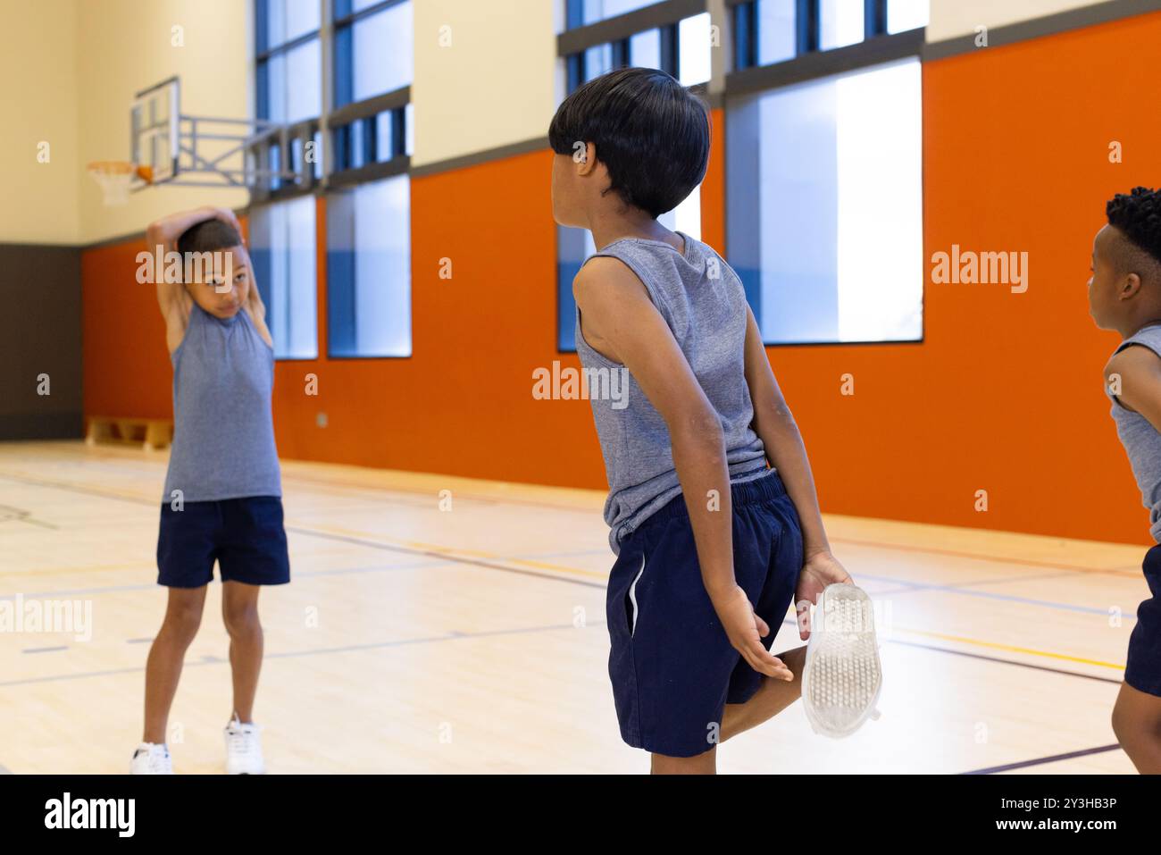 In school gym, multiracial boys stretching and warming up for physical ...