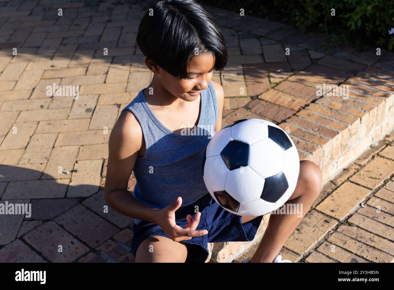Holding soccer ball, boy sitting on brick pavement, enjoying outdoor ...