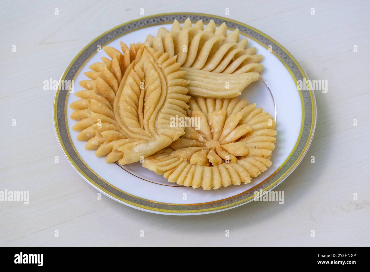 Crispy Nakshi Pitha on a white plate on a light wooden surface. It is a ...