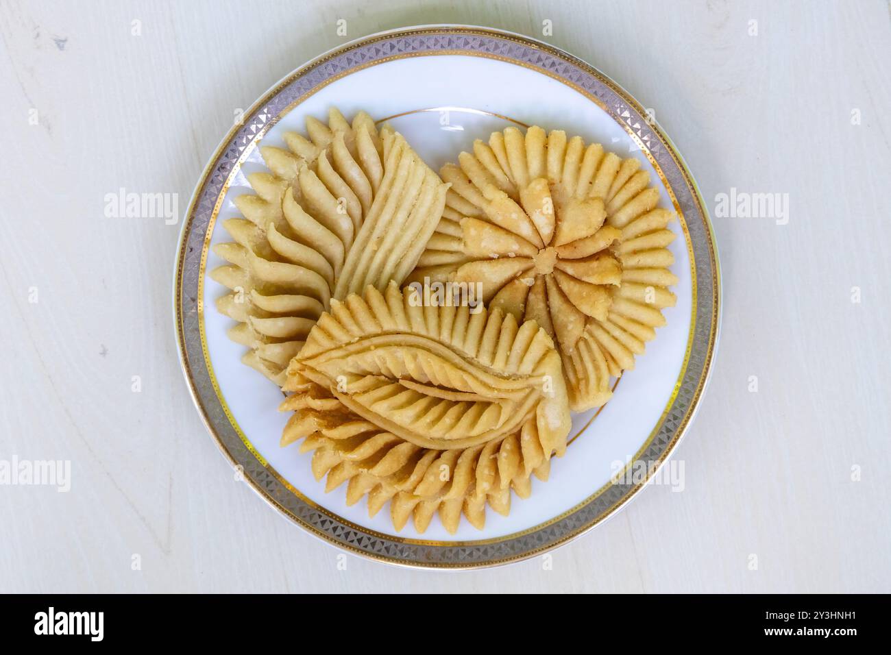 Crispy Nakshi Pitha on a white plate on a light wooden surface. It is a ...