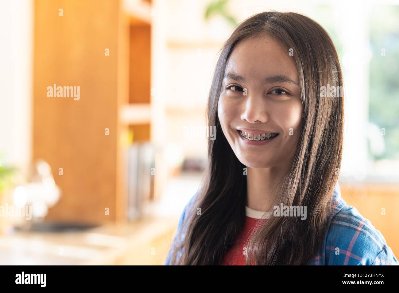 At home, Smiling young asian woman with braces standing in bright kitchen, looking at camera ...