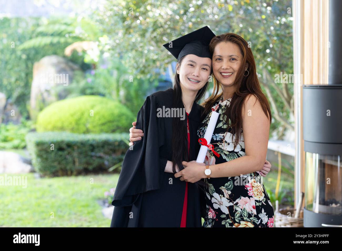 In garden, Graduating, asian daughter in cap and gown hugging smiling ...