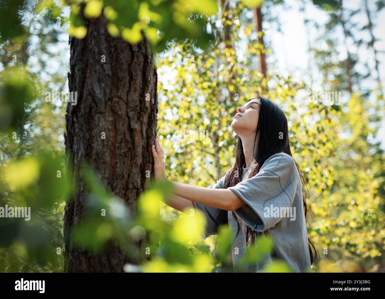 A young girl hugs a tree in the forest. Hugging and touching trees to ...