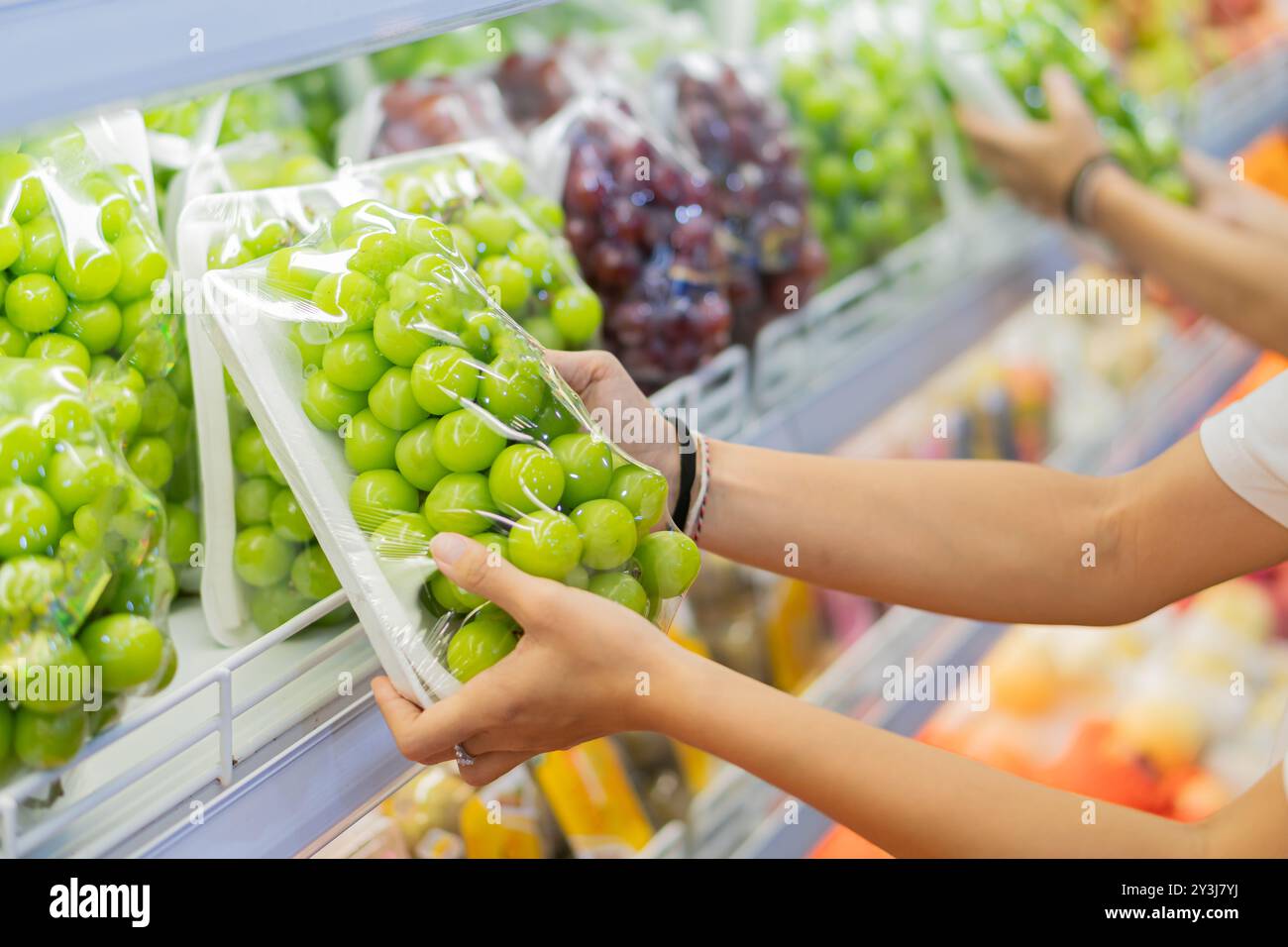A person selecting a pack of green grapes from a refrigerated display ...