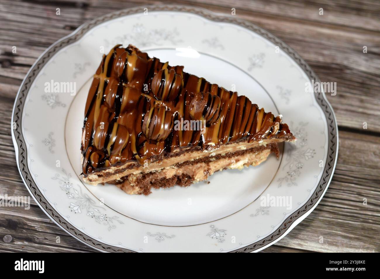 A chocolate triangular spongy cake piece filled and topped with layers ...