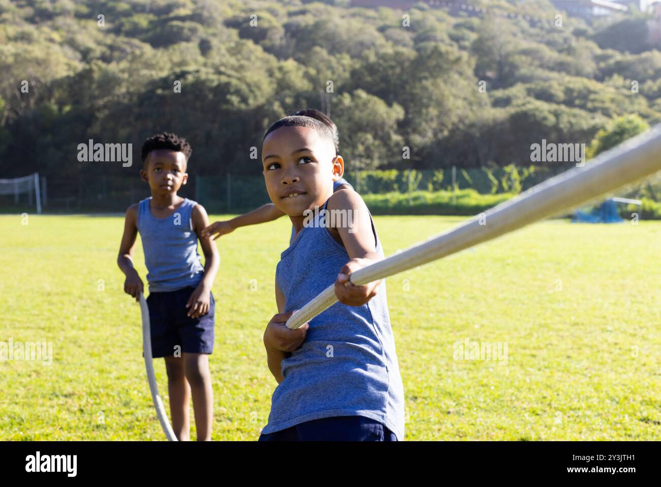 Playing tug-of-war, multiracial boys in school sports field enjoying ...