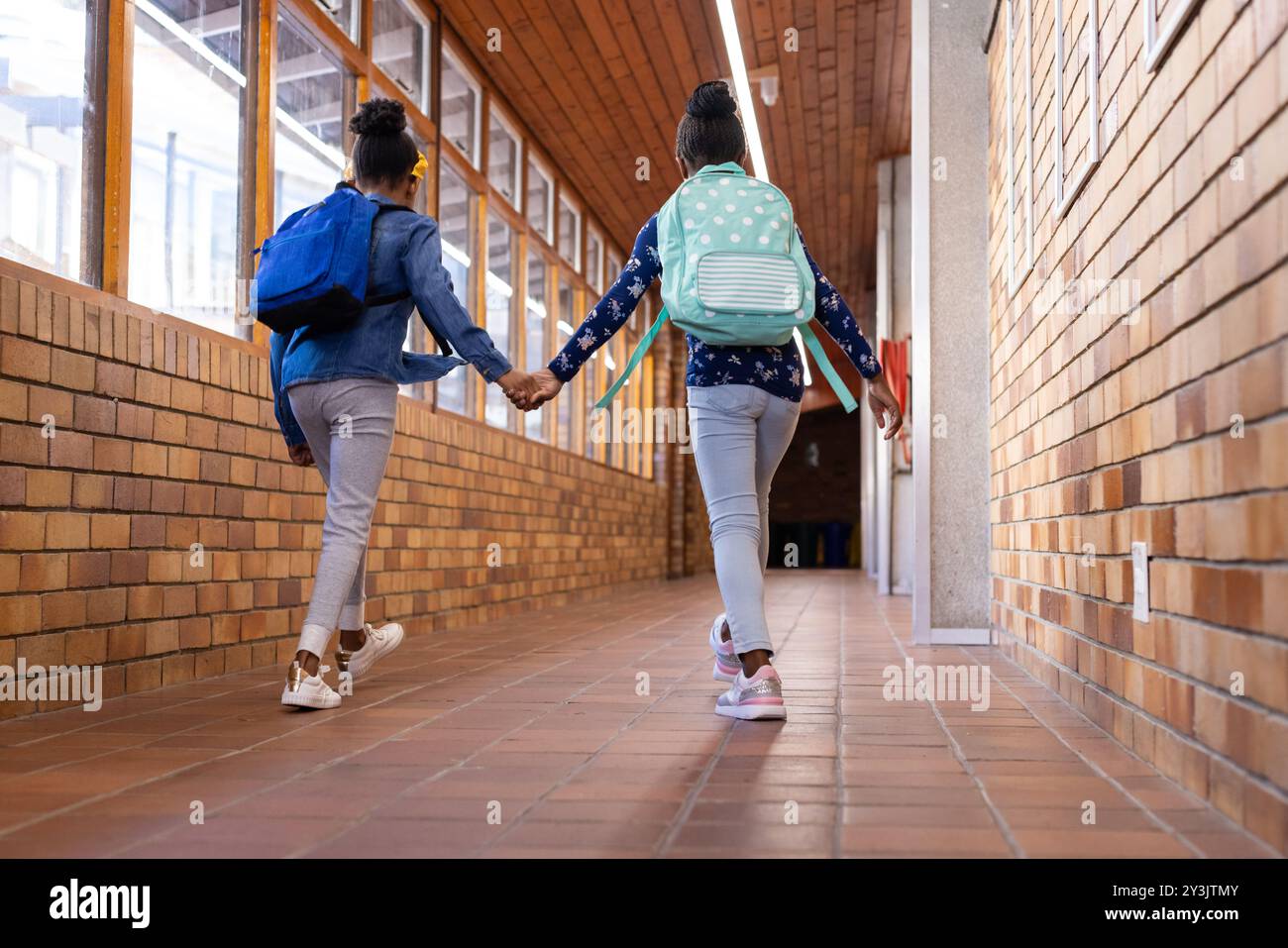 Walking in school hallway, two african american girls holding hands and ...