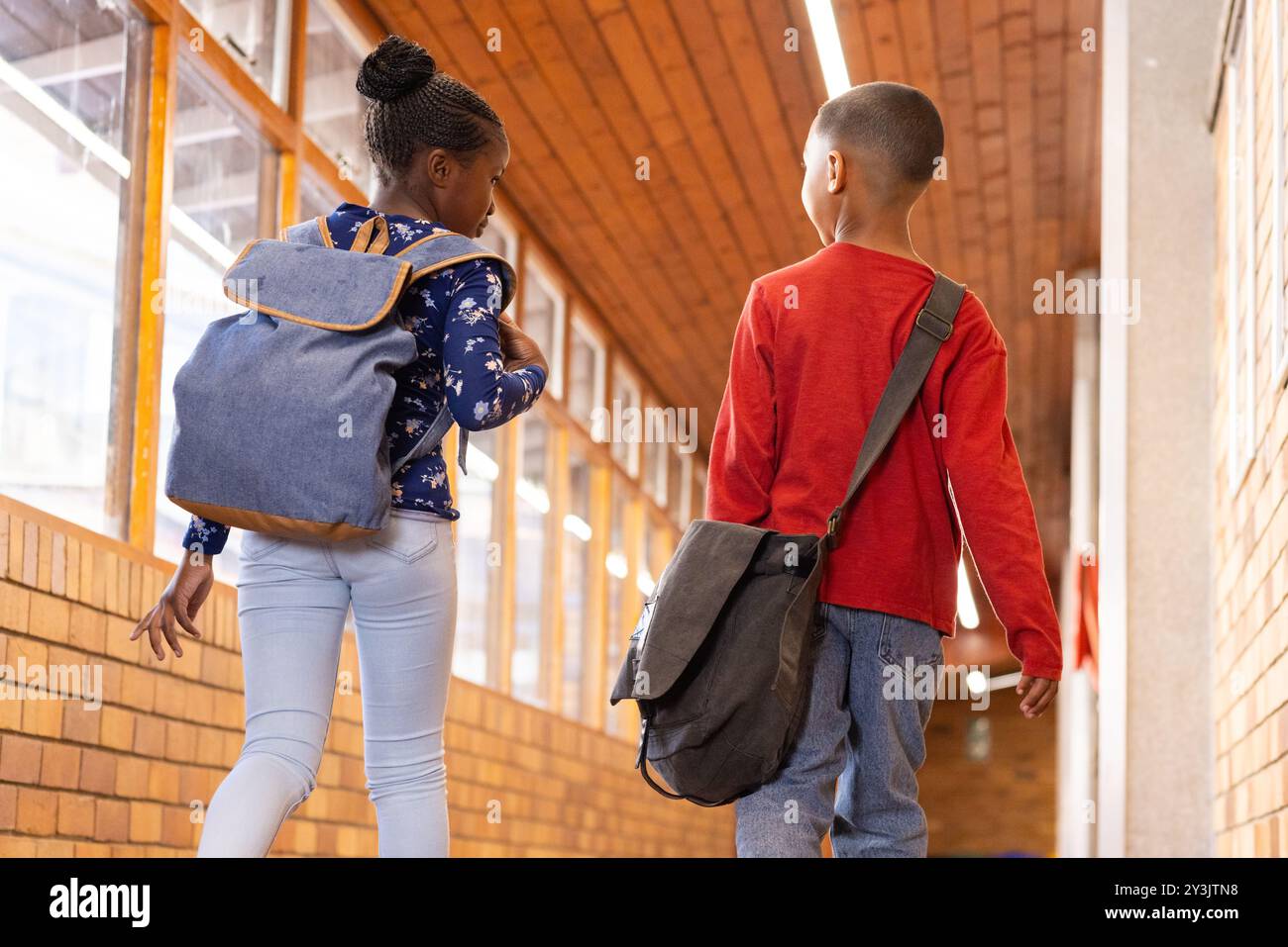 Walking in school hallway, two multiracial boy and girl with backpacks ...