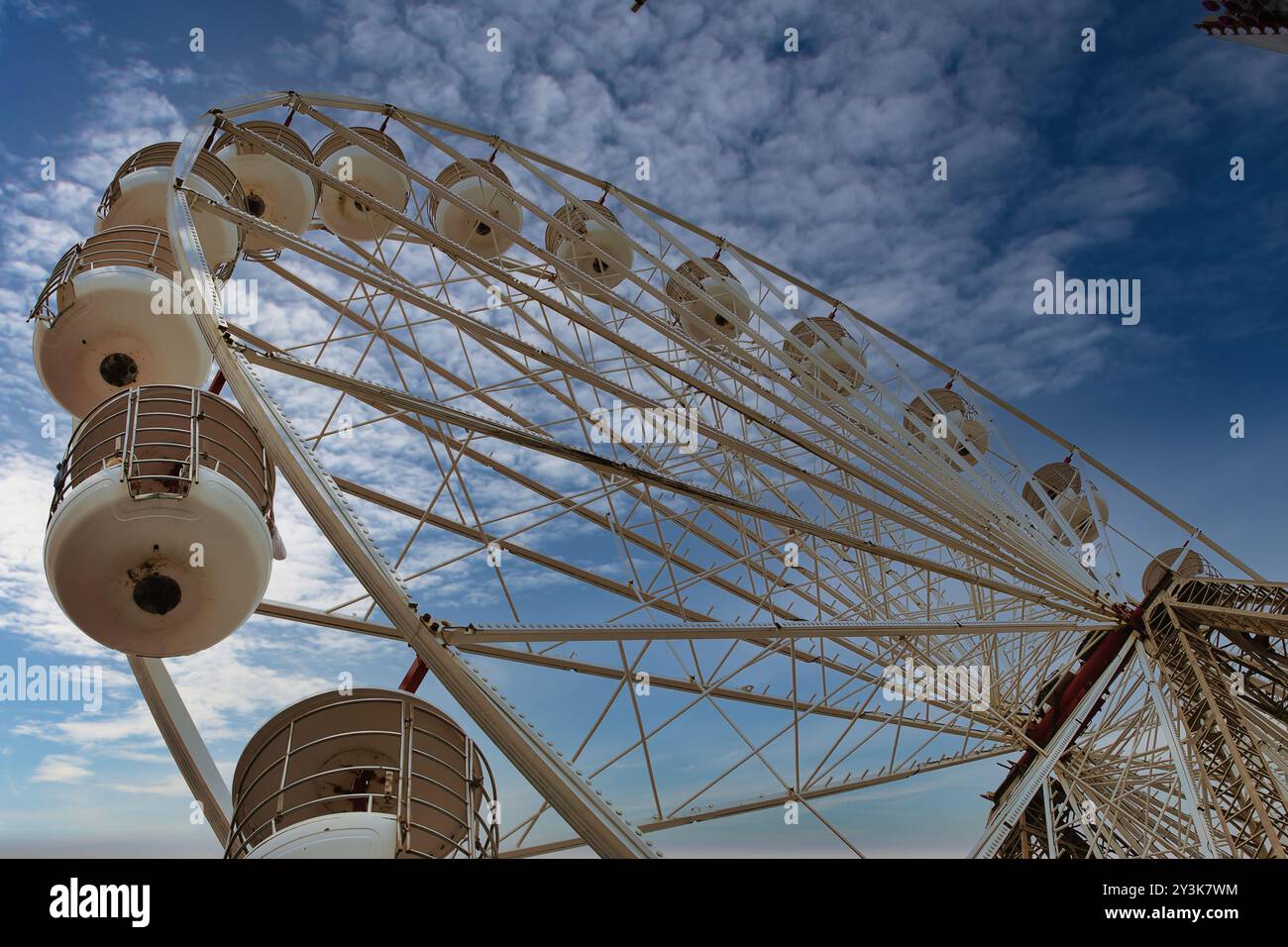 A close-up view of a large Ferris wheel against a blue sky with clouds ...
