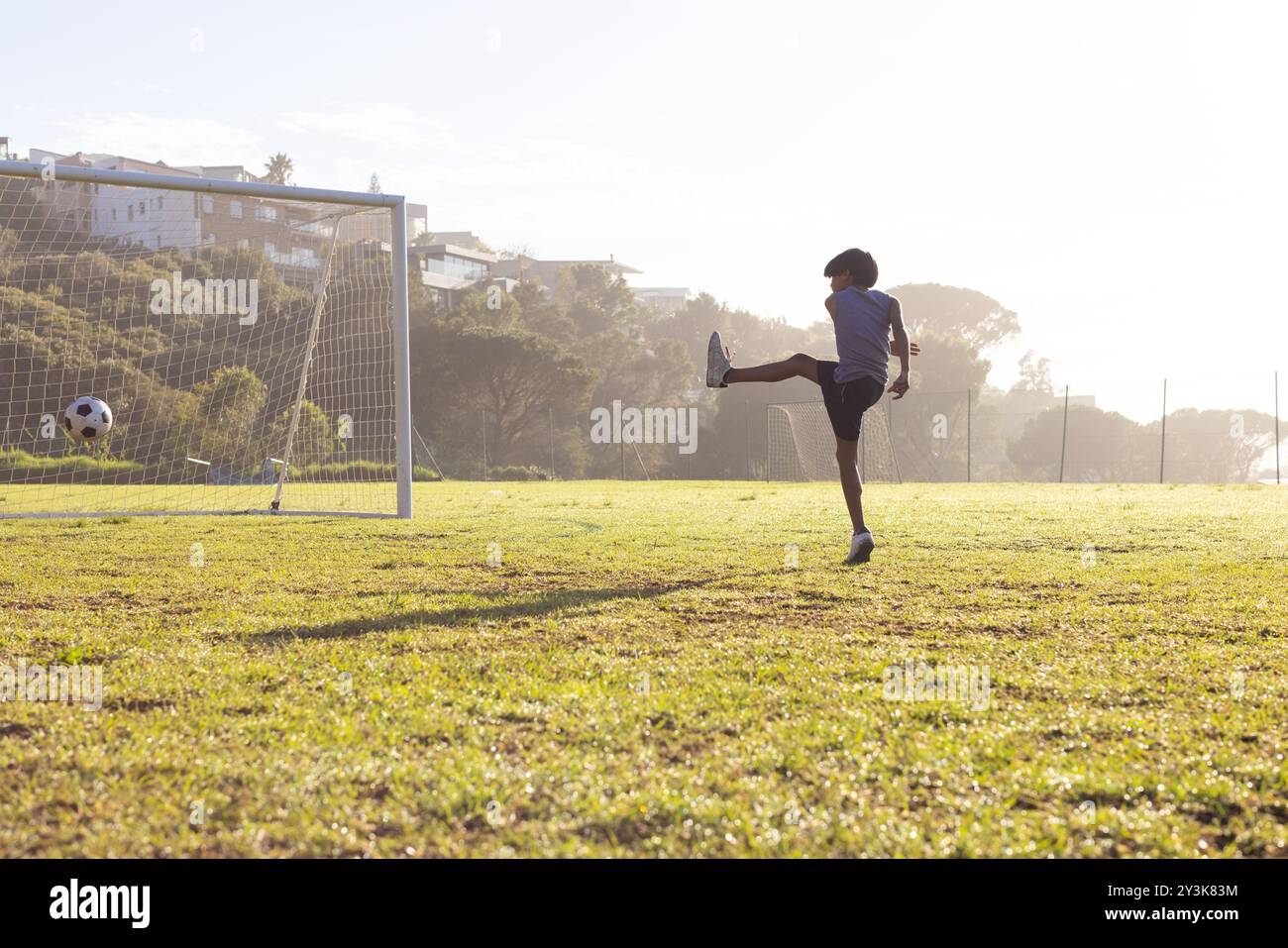 Outdoors, Kicking soccer ball towards goal, boy playing on school field ...