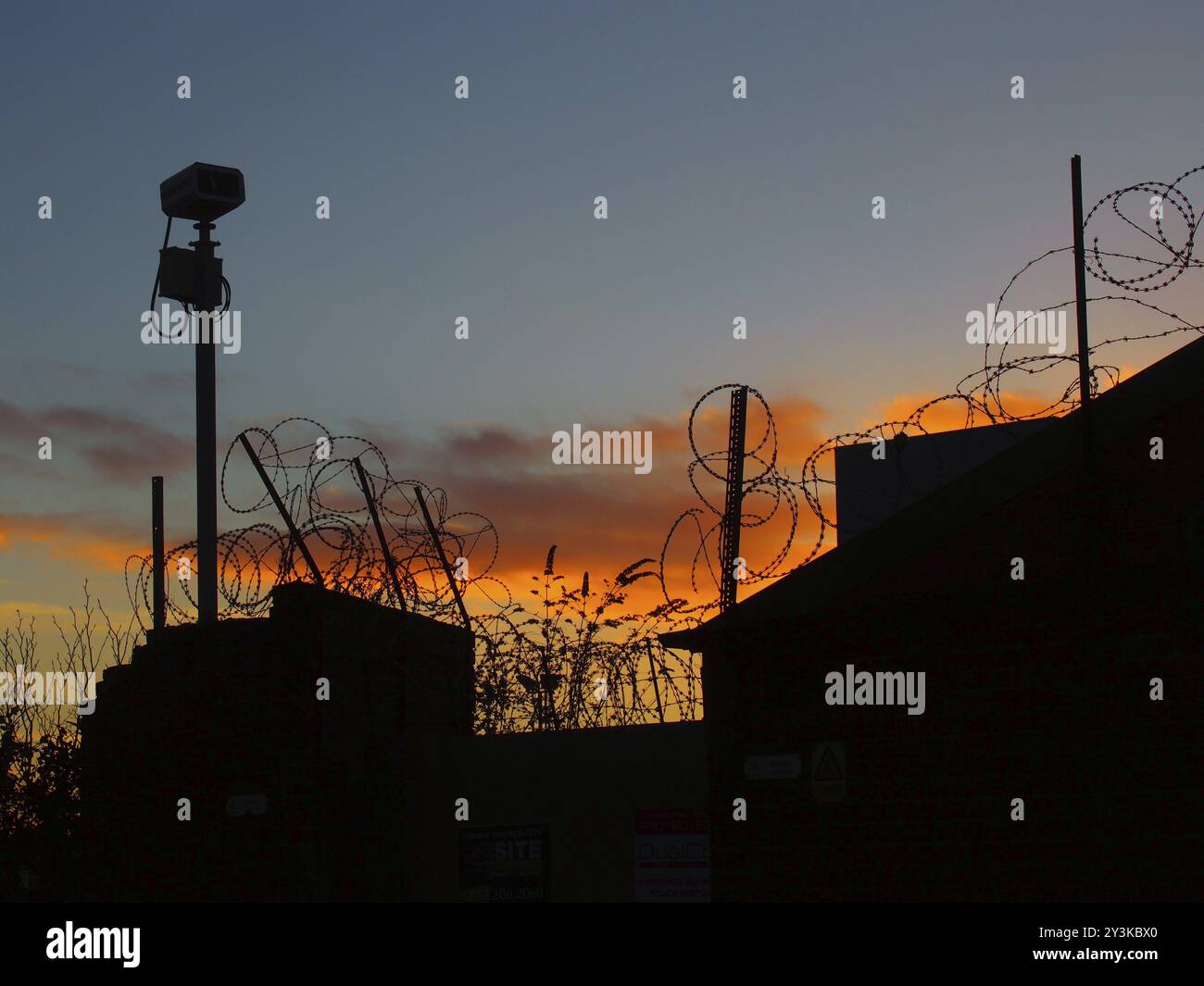 Barbed wire on a wall and security camera with evening sky and sunset ...