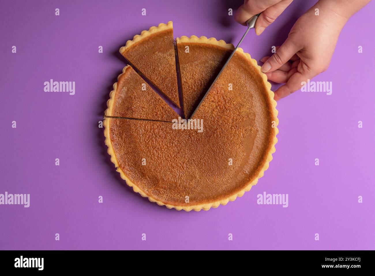 Woman hands slicing a pumpkin pie on a purple background. Minimalist ...