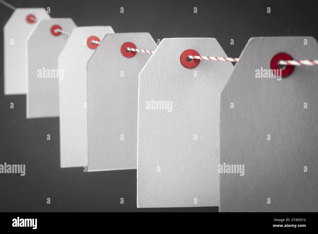 Blank paper tags line up on a red-white string against a dark ...