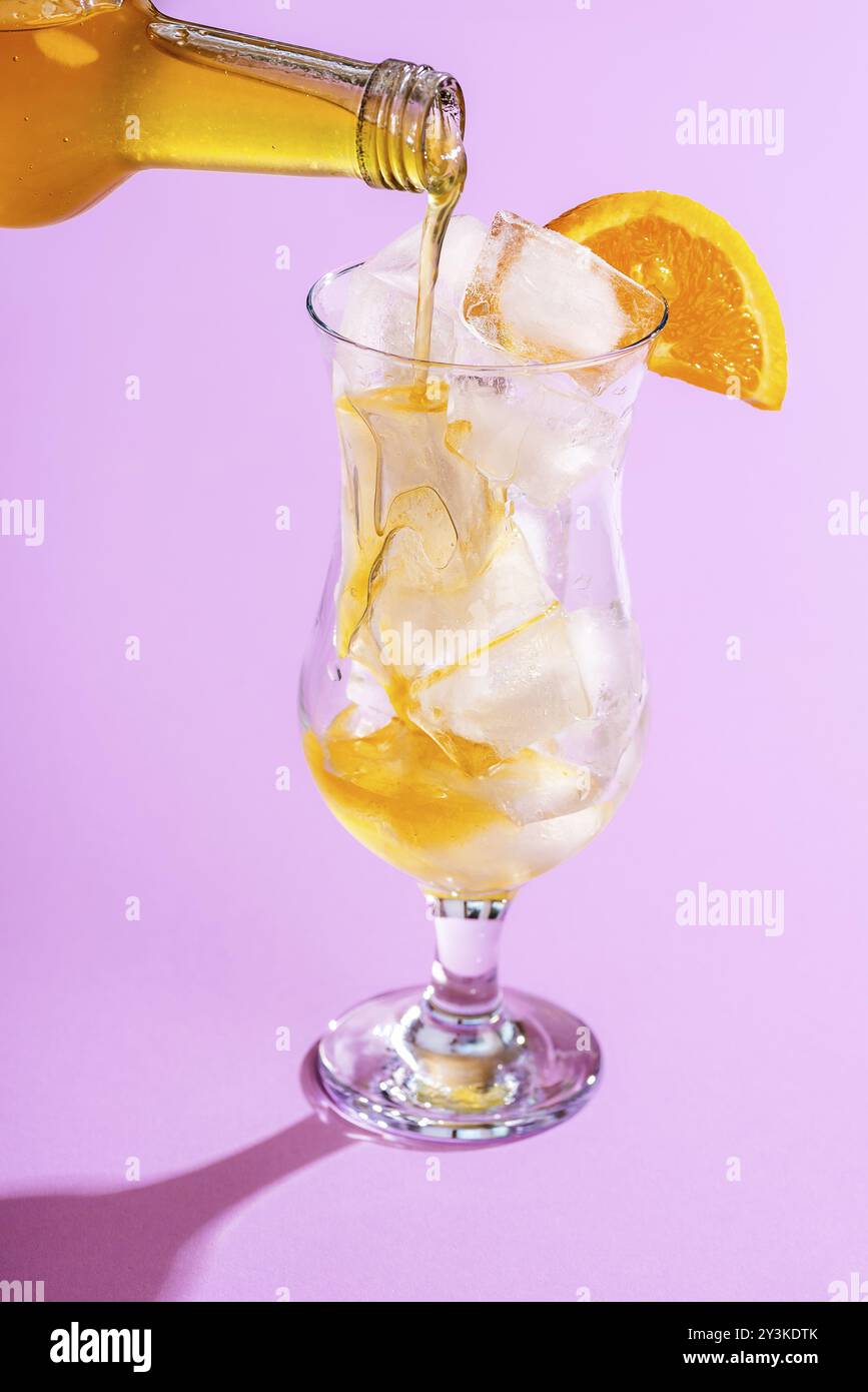 Preparing a summer cold drink by pouring orange syrup over ice cubes in ...