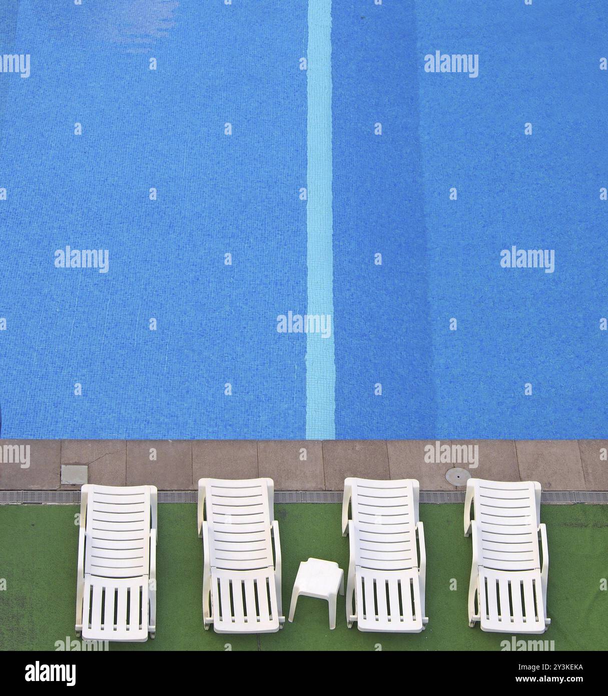 Aerial view of white sunbeds at the side of a blue swimming pool with ...