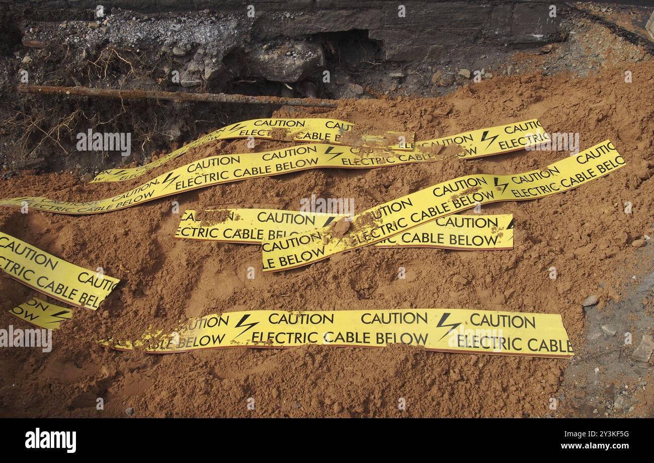 Yellow tape signs warning of buried electric cable below in a trench ...