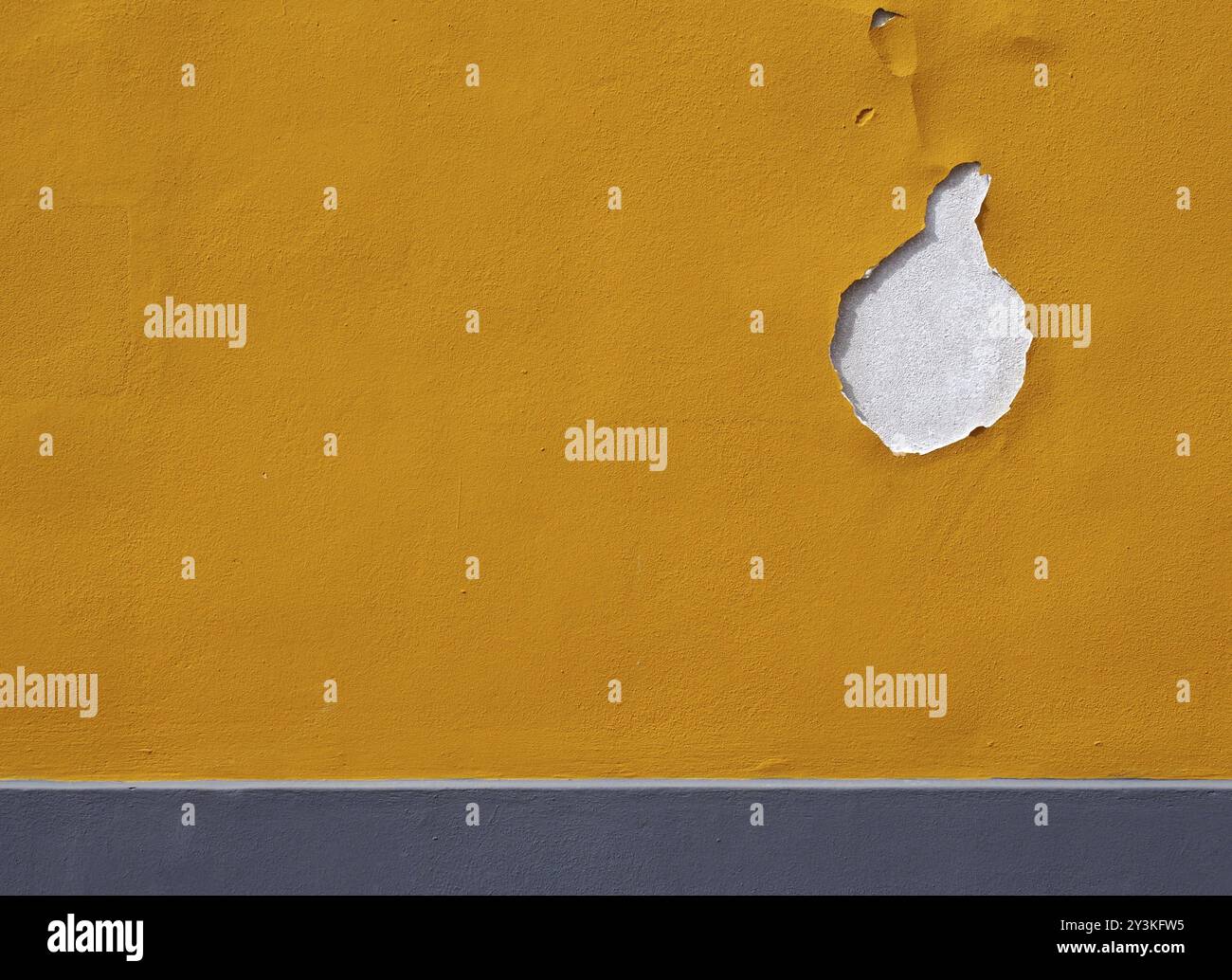 Bright yellow textured paint on an external wall with cracks and hole ...