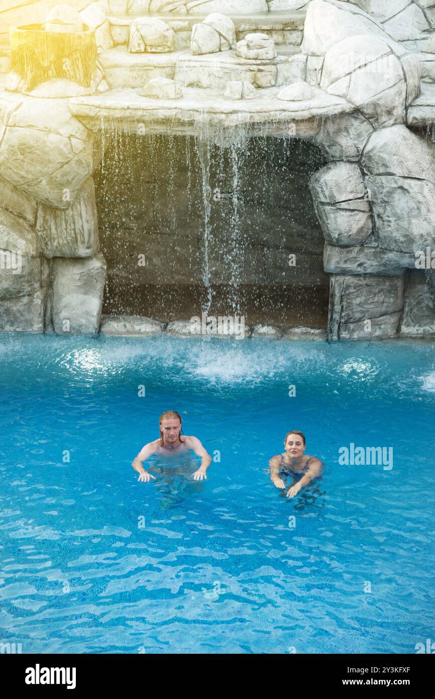 A man and a woman swimming in the pool with a waterfall backdrop at a ...