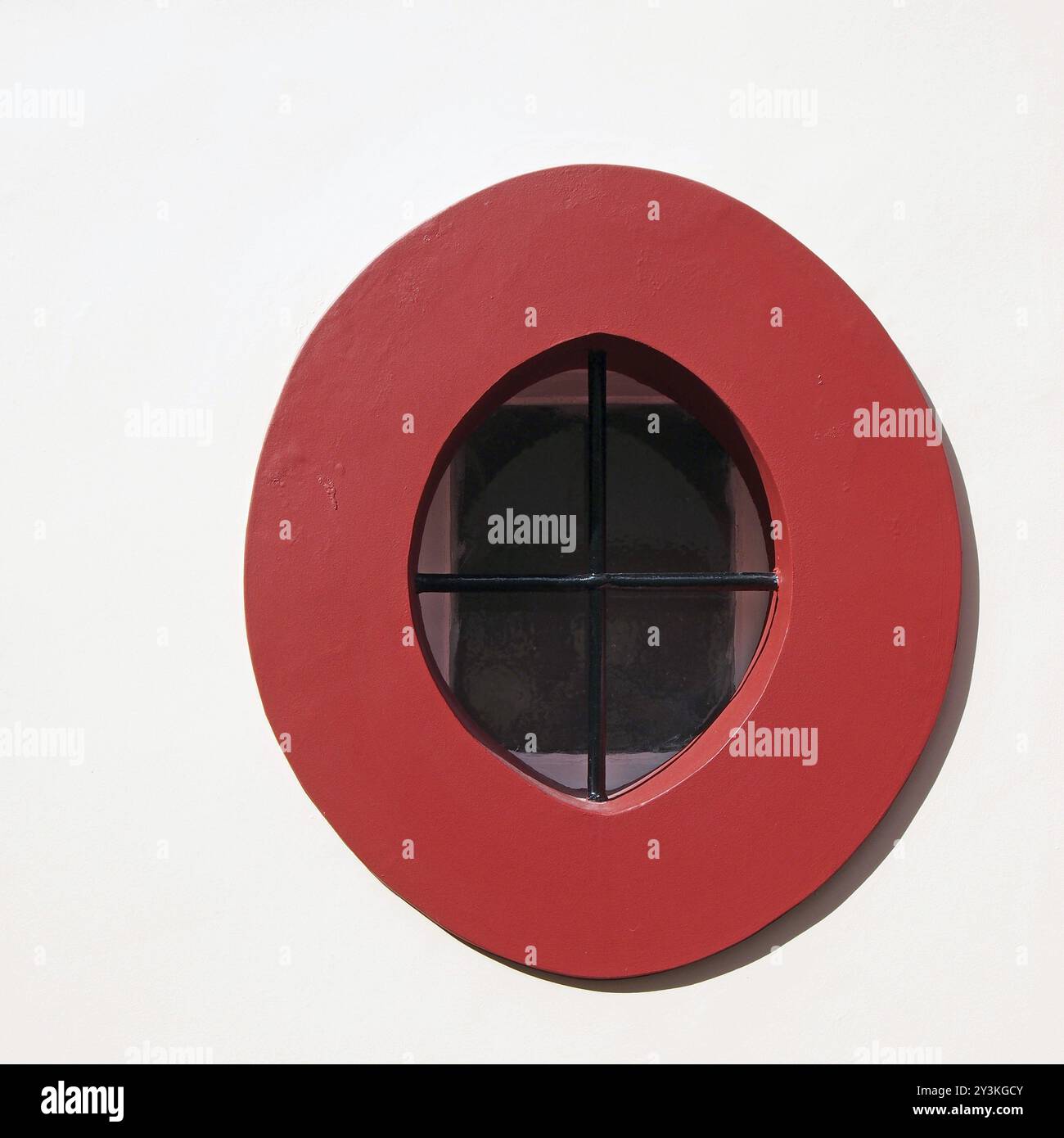 Bright red stone oval window frame in a white wall with black metal ...