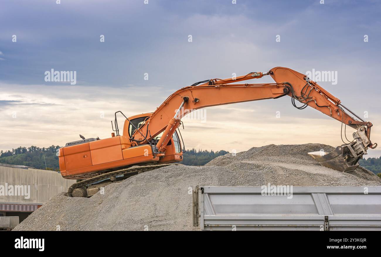 Orange excavator, climbed on a ballast pile, loading material in a ...