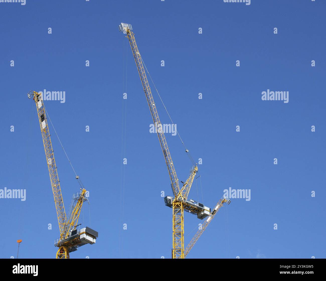Two tall yellow construction cranes working against a blue sky Stock ...
