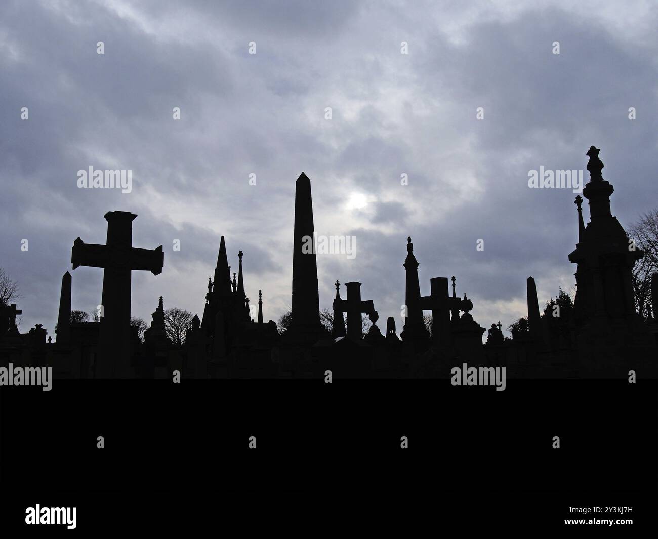 Old gothic style gravestone in silhouette with tall memorials and ...