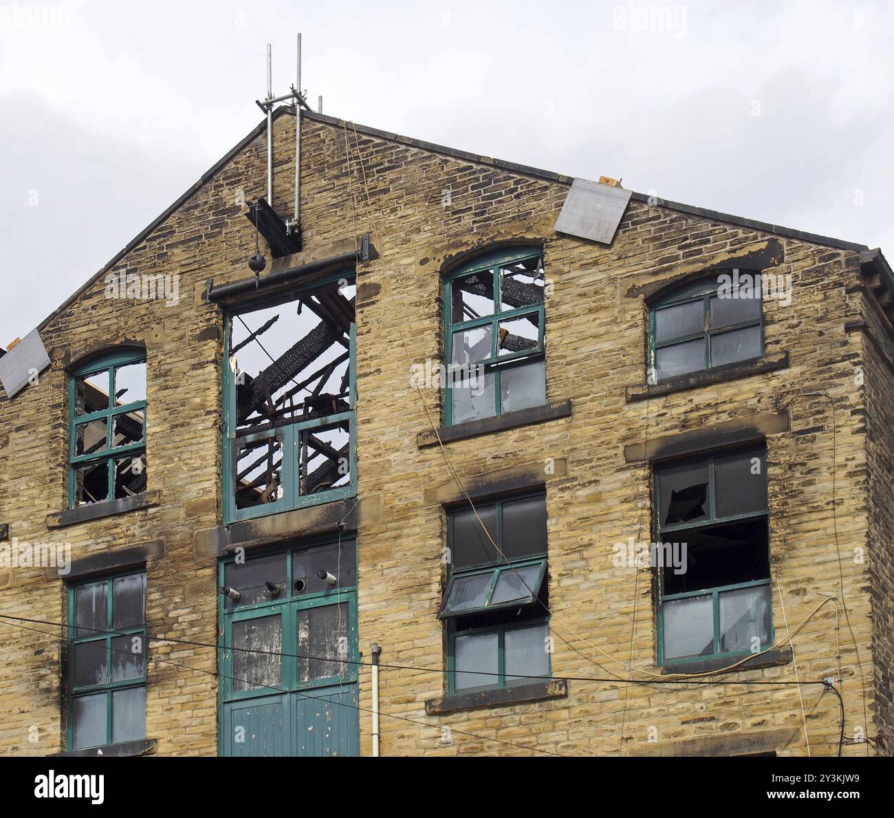 The broken roof and broken windows in a large burned out old industrial building after a fire ...