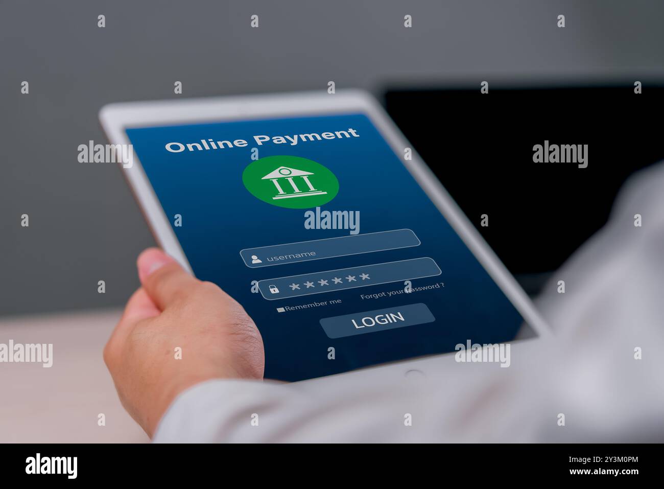 Hand holding a tablet displaying an online payment login screen ...