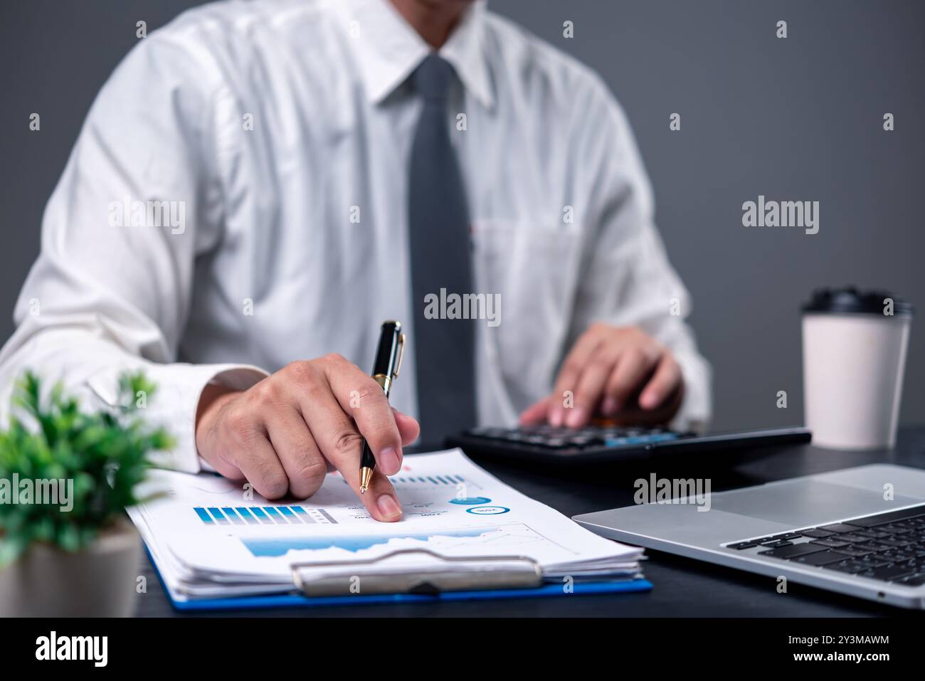Businessman analyzing financial documents, using laptop and calculator. Focus on data accuracy ...