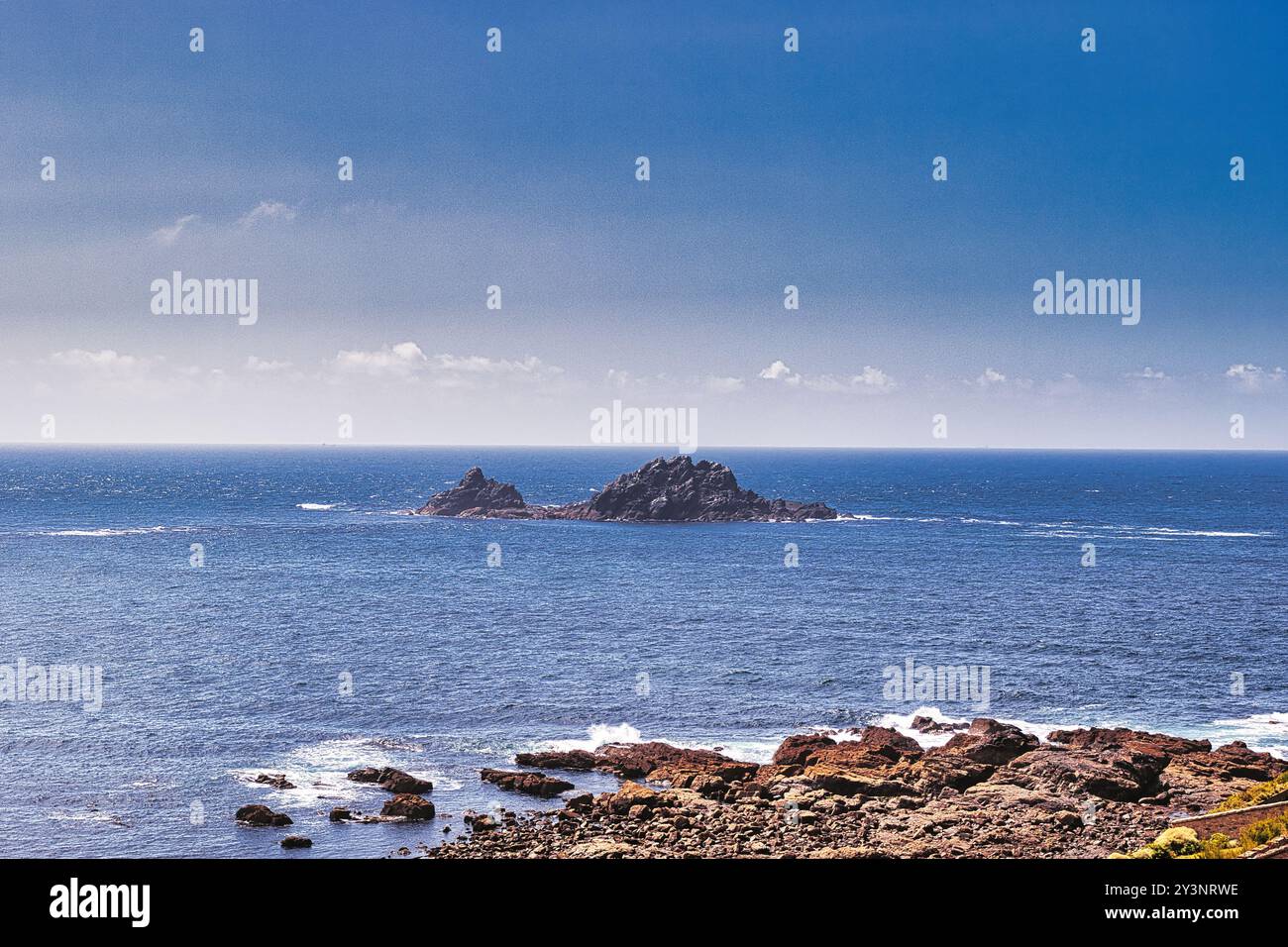 A serene coastal landscape featuring a rocky shoreline and a distant ...