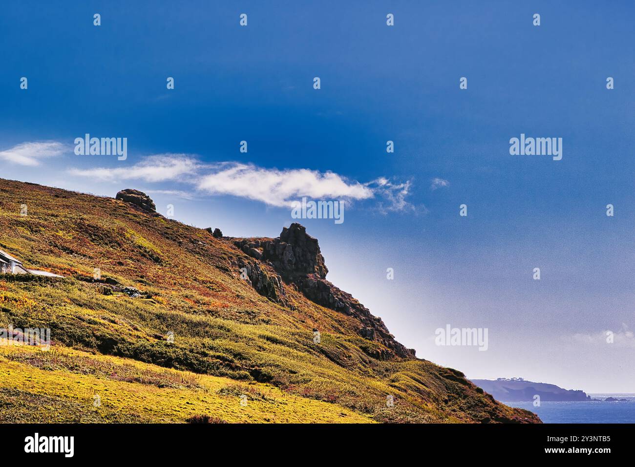 A scenic coastal landscape featuring a grassy hillside with rocky ...