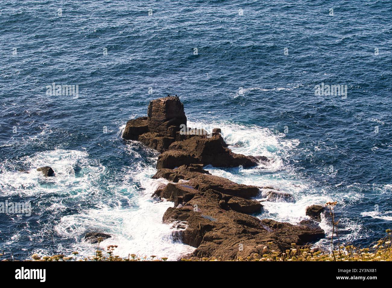 A rocky outcrop in the ocean with waves crashing against it. The water ...