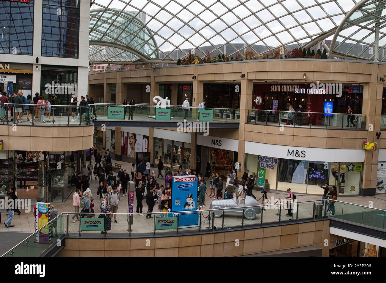 A busy shopping mall with multiple levels, featuring a glass roof ...