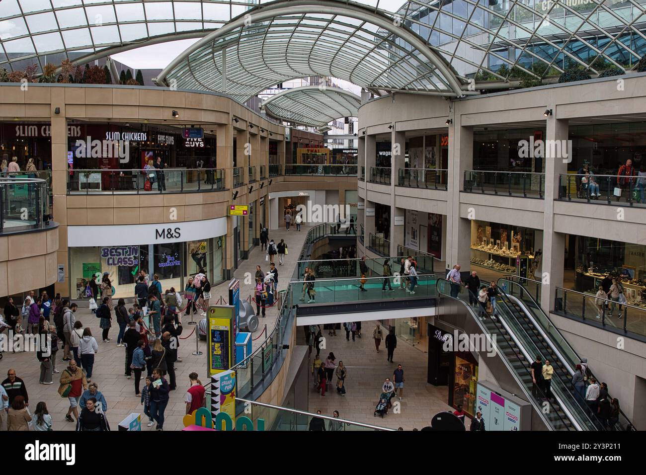 A bustling shopping mall with multiple levels, featuring various retail stores and shoppers. The ...