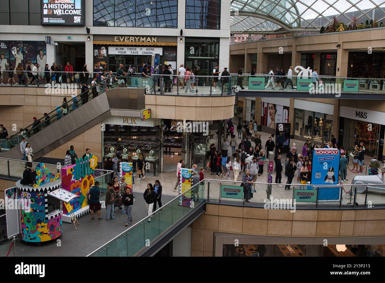 A bustling shopping mall with multiple levels, featuring colorful displays and a large crowd of ...