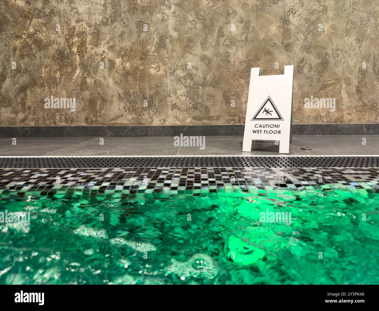 Safety sign with phrase Caution wet floor stands next to the jacuzzi ...