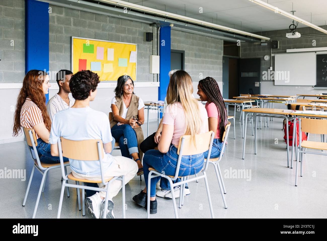 Young group of teenage students discussing in classroom with teacher ...