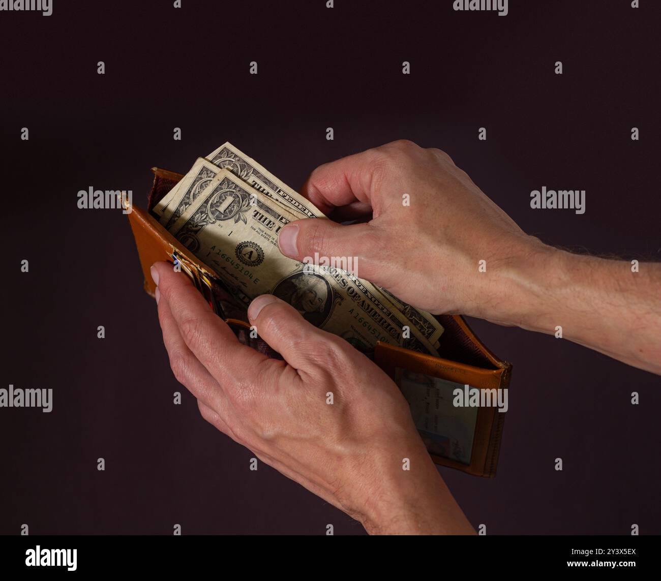 A man's hands hold open an old wallet with only three dollars left ...