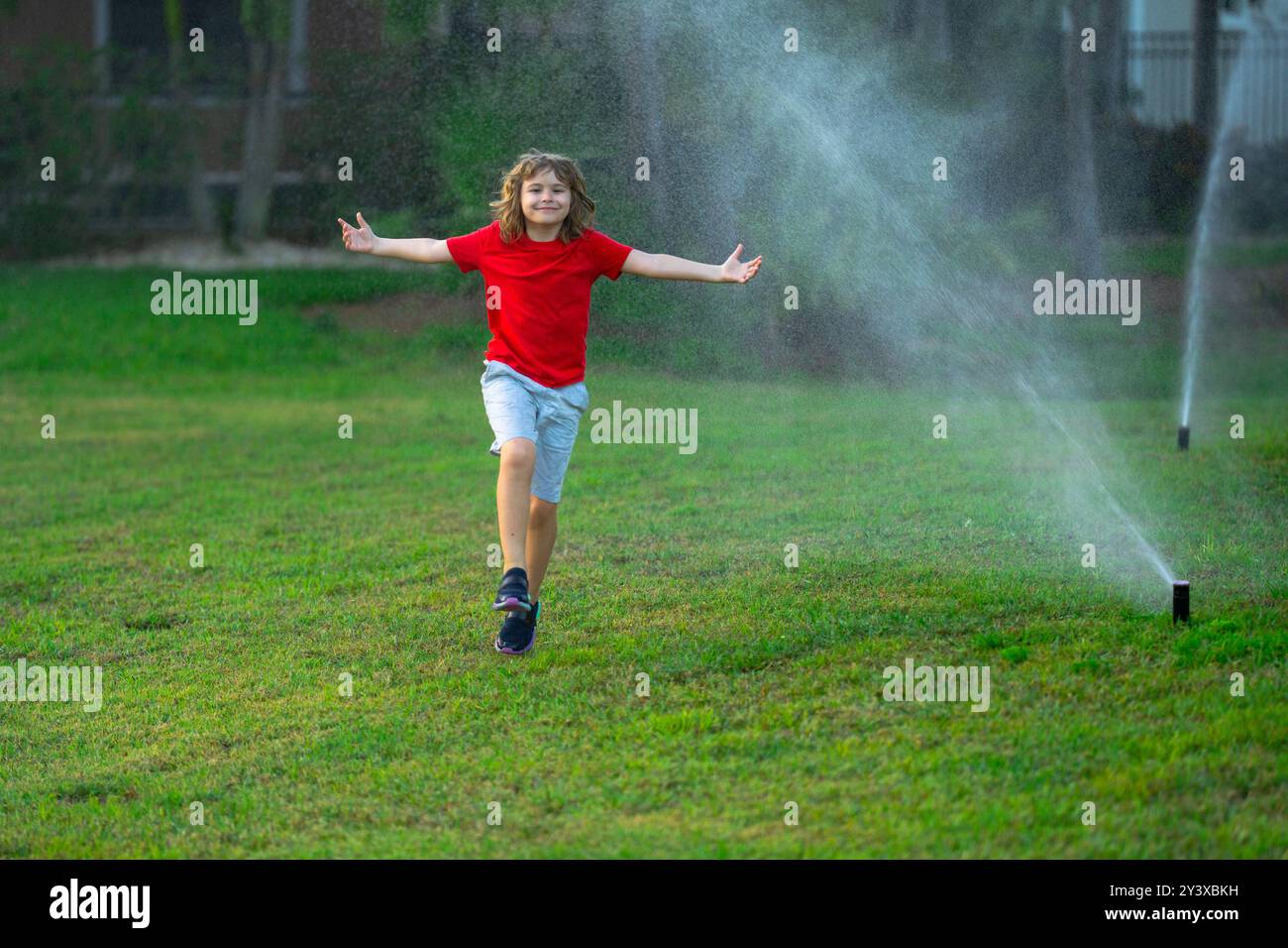 Kid play in garden near irrigation watering sprinkler system. Watering ...