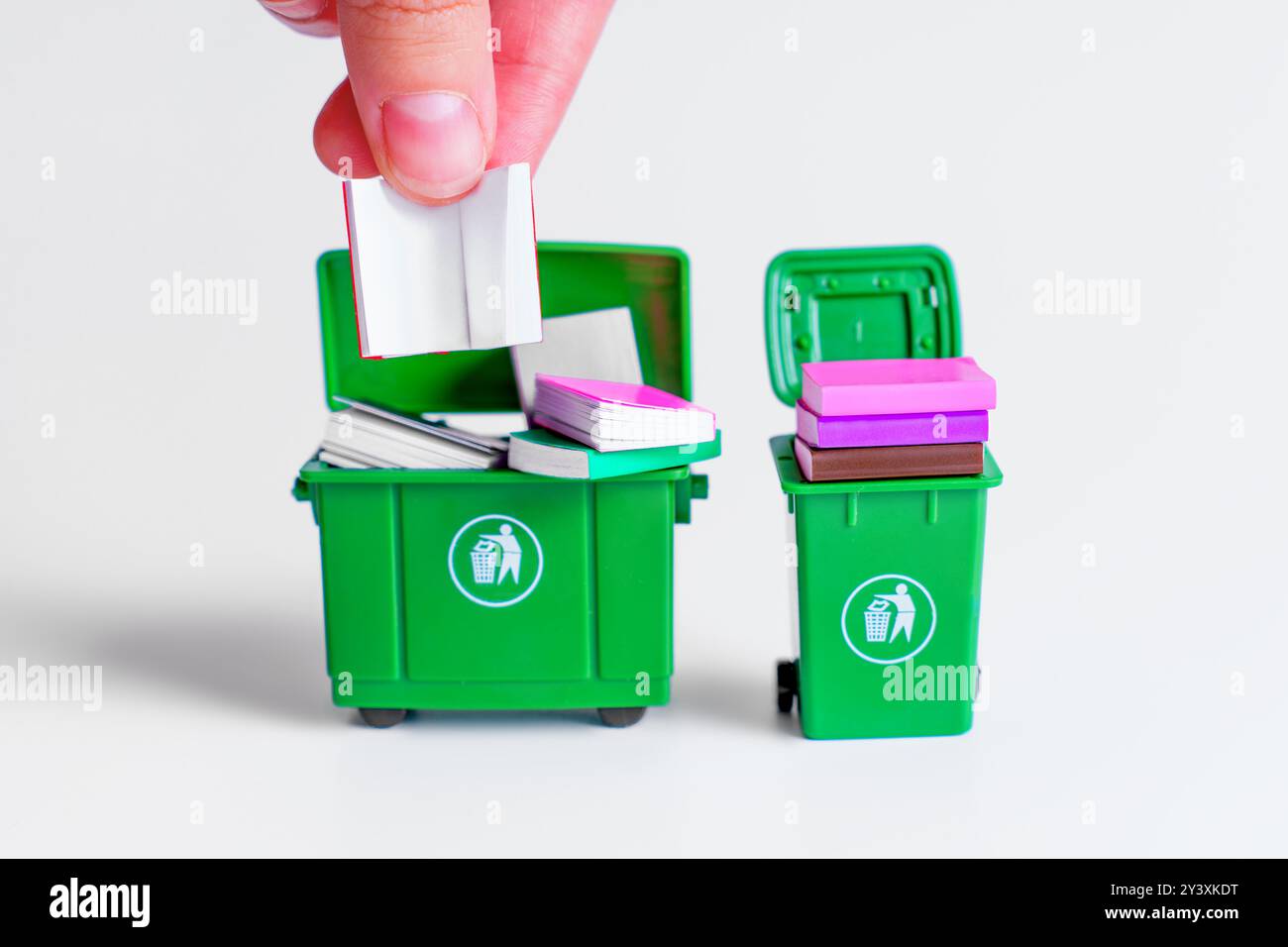 Miniature books being discarded into green trash bins, showcasing waste ...