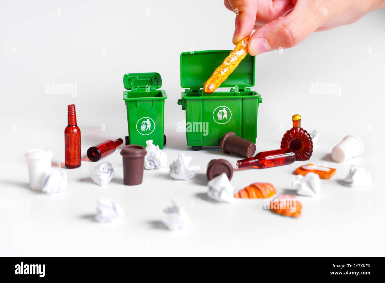 Hand disposing trash into miniature green bins. Scene filled with ...